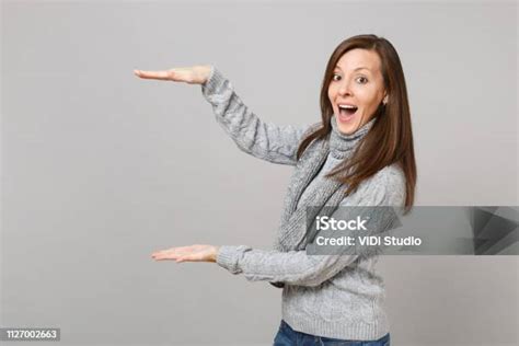 회색 스웨터 스카프 회색 배경에 고립 된 수직 작업 크기를 보여주는 몸짓에 흥분된 여자 건강 패션 라이프 스타일 사람 감정 추운 계절 개념입니다 복사 공간을 비웃는 다