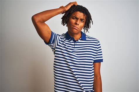 고립 된 흰색 배경 위에 서있는 줄무늬 파란색 폴로를 입은 공포를 가진 아프로 남자는 혼란스럽고 질문에 대해 궁금해합니다 의심의 여지가 머리에 손으로 생각 펜시브 개념