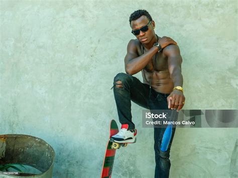 젊은 매력적이 고 잘 생긴 흑인 아프리카계 미국인 남자 맞는 근육 질의 몸 및 여섯 팩 개최 야구 방망이와 스케이트 보드 포즈 멋진 도시 늠 름 한와 나쁜 소년 태도에 거리