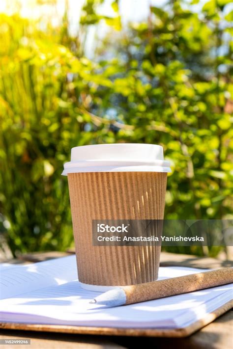 나무 벤치에 빈 종이 노트북이 있는 크래프트 종이에 커피 또는 차가 있는 에코 재활용 종이컵 야외에서 일하는 연구의 개념 커피를 가져 가라 텍스트 공간을 복사합니다 일회용