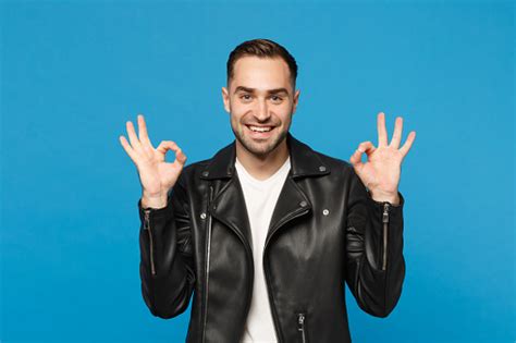 블랙 가죽 자 켓 흰색 T 셔츠에 잘생긴 세련 된 젊은 수염 남자 블루 벽 배경 스튜디오 초상화에 고립 된 카메라를 찾고 사람들은 진심으로 감정 라이프 스타일 개념입니다