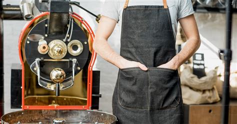 앞치마를 입은 바리스타가 로스터 기계 근처에 서 있는 주머니에 손을 넣고 있습니다 사진 Unsplash의 사업 이미지