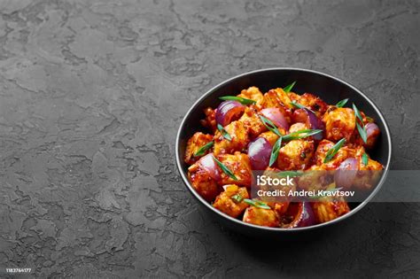 어두운 슬레이트 배경에 검은 그릇에 Schezwan 파니어 Schezwan Paneer는 튀긴 파니에 치즈 양파 슈즈완 소스를 곁들인 인도 중국 요리입니다 공간 복사 0명에