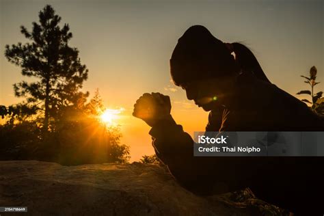 At Sunrise The Silhouette Of A Christian In Prayer Hands Lifted In