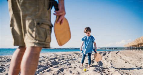 알아볼 수 없는 아버지가 라켓과 공으로 모래 부리 위에서 야외에서 놀고 있는 작은 소녀 사진 Unsplash의 가족 이미지