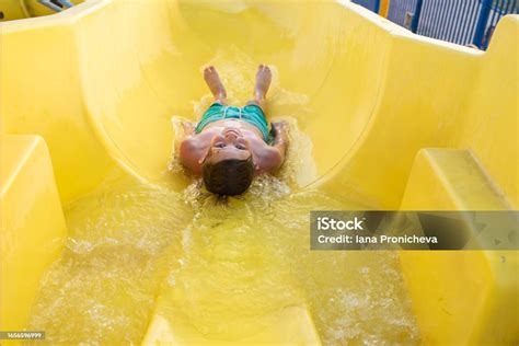 행복한 아이는 워터 파크에서 노란 워터 슬라이드를 미끄러집니다 즐거운 10 살짜리 소년은 언덕을 타고 워터 파크에서 즐거운 시간을 보냅니다 워터 파크에 대한 스톡 사진 및