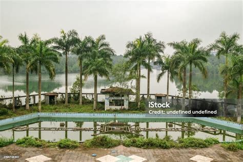 야자수 호수 먼 구조물이 있는 황량한 리조트 탁한 물과 쓰레기로 가득 찬 수영장 맞은편 해안에는 나무 사이에 호텔 같은 건물이 있습니다 베트남 후에에 버려진 워터파크