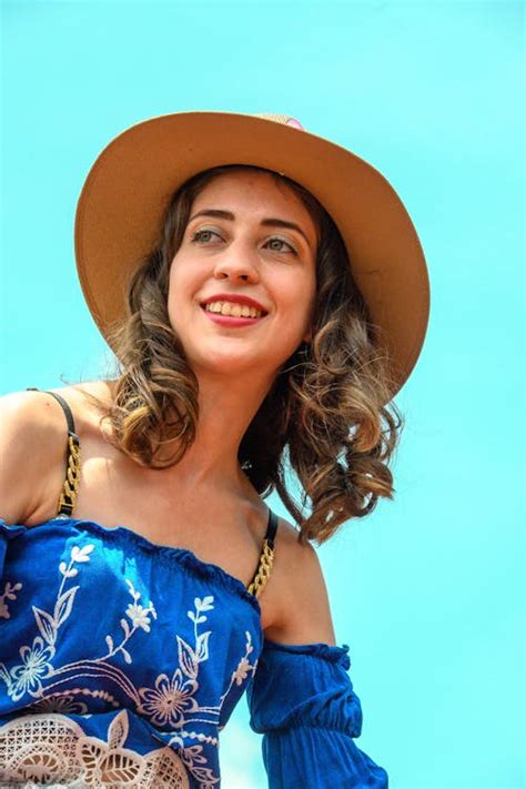 갈색 머리 모델 모자 미소 짓는 수직 쐈어 스튜디오 촬영 여성 초상화 파란색 배경 패션 사진에 관한 무료 스톡 사진