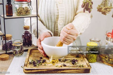 전통적인 약용 차를 위해 다양한 말린 허브를 박격포와 유봉을 혼합한 여성 약초학자의 전망을 클로즈업합니다 배경에 유리 항아리에 말린 허브 부엌에 대한 스톡 사진 및 기타