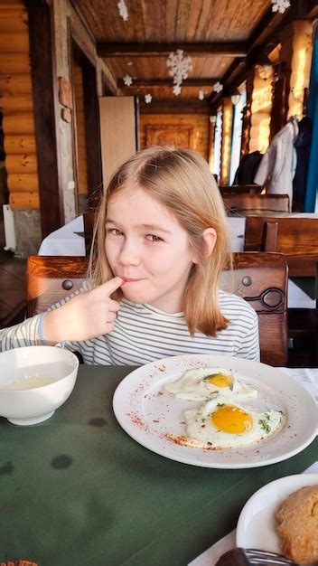 Premium Photo Cute Girl Licks Her Finger At Breakfast With Scrambled Eggs