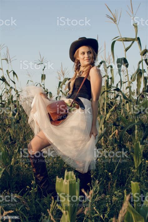 젊은 여성이 입고 있는 카우걸 일몰에 농부의 작물 분야에 서 고 건초 더미에 달려있다 갈색 머리에 대한 스톡 사진 및 기타 이미지 갈색 머리 건초 식물 건초 재배