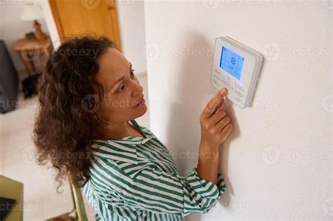 Woman Adjusting Smart Home Thermostat On Wall For Temperature Control Stock Photo At