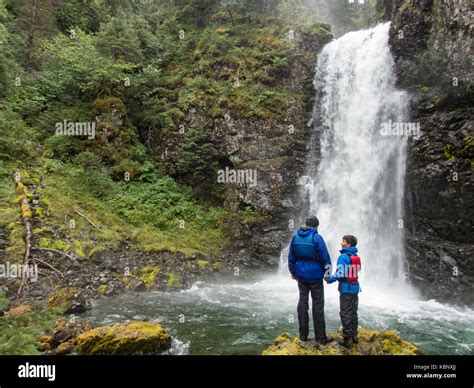Father And 10 Year Old Son Holding Hands And Discovering Remote Waterfall During Kayak Trip In