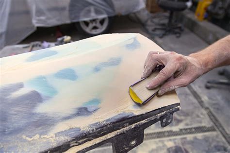 한 남자가 자동차 수리점에서 연마용지를 연마하는 일의 도움으로 사고 후 그림을 그리기 위해 차체 요소를 준비합니다 충돌 후 복구