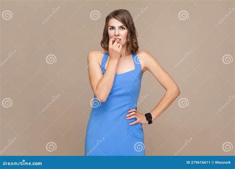 Anxious Nervous Woman With Wavy Hair Bites Finger Nails With Puzzlement Keeps Hand On Hips