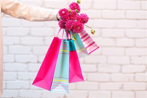 벽돌 배경에 꽃과 쇼핑 백을 들고 여성의 손 여자의 날 발렌타인 데이 생일 파티를위한 준비 공간을 복사합니다 종이 선물 가방 의 무리 선물 가방에 대한 스톡 사진 및 기타