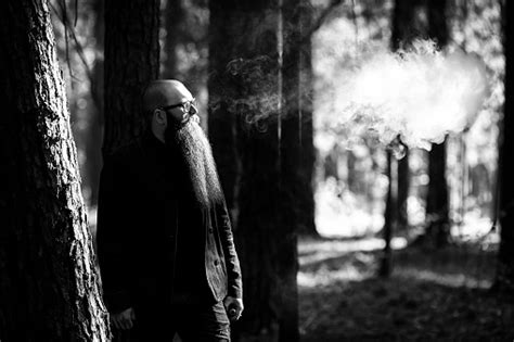 Vape 수염 남자 안경에 매우 긴 수염을 가진 성인 흰색 짧은 머리 남자는 어두운 숲에서 외부 전자 담배를 연기 나쁜 습관 건강하지 못한 생활방식에 대한 스톡 사진 및