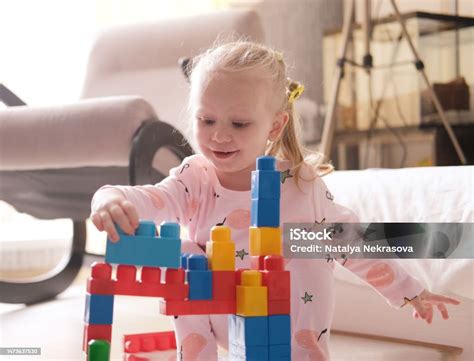 웃고 있는 어린 아이 화려한 큐브를 가지고 노는 금발의 미취학 아동 분홍색 잠옷을 입고 바닥에 앉아 집에 큰 창문이 있는 햇볕이