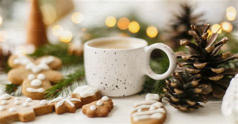 수제 진저 브레드 쿠키와 솔방울 장식 전나무 가지 흰색 나무 테이블에 따뜻한 조명이 있는 세련된 흰색 컵에 담긴 뜨거운 커피