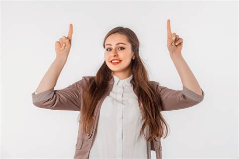 이것 보세요 쾌활한 사랑스러운 갈색 머리 여자는 빛나는 미소로 손가락을 가리키고 기쁘게 보이고 좋은 제안에 만족하고 흰색 스튜디오 배경에 서 있다 1에 대한 스톡 사진 및