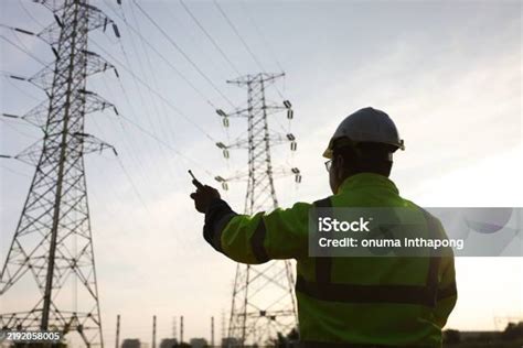 녹색 안전 재킷과 안전모를 쓴 고위 고전압 엔지니어가 전봇대 아래 발전소에서 노트북과 워키토키를 작업하고 있습니다 건설 프레임에 대한 스톡 사진 및 기타 이미지 Istock