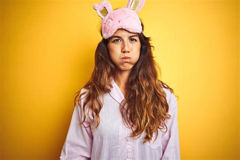 잠옷과 수면 마스크를 입고 노란색 고립 된 배경 퍼핑 뺨에 서있는 젊은 여성 재미있는 얼굴 공기 미친 표정으로 입이 팽창 가득