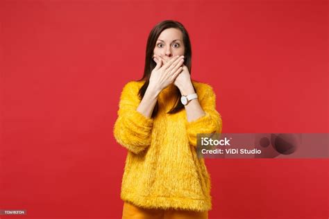 충격의 초상화는 스튜디오에서 밝은 빨간색 벽 배경에 고립 된 손으로 입을 덮고 노란 모피 스웨터에서 젊은 여자를 무서 워 사람들은 진심으로 감정 라이프 스타일 개념입니다