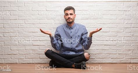 젊은 성인 남자 백색 벽돌 벽 우 둔 하 고 혼란 스 러 워 식으로 발생 하는 손과 팔에 앉아 의심 개념입니다 감정에 대한 스톡 사진 및 기타 이미지 Istock