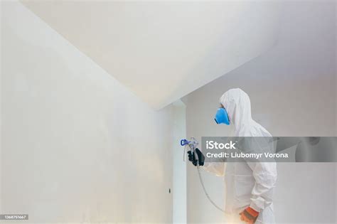 공기없는 스프레이 페인트 작업자는 흰색으로 공기가 없는 스프레이로 벽을 페인트하고 숙련된 작업자가 기계식 공기 도구로 표면에 페인트를 분사합니다 벽에 대한 스톡 사진 및