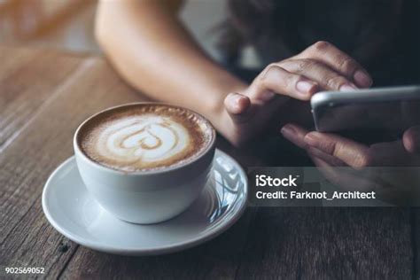 근접 촬영 이미지는 여자의 손을 잡고 를 사용 하 여 나무 테이블 빈티지 카페에서 라 떼 커피 컵과 스마트 폰에서 가리키는 스마트폰에 대한 스톡 사진 및 기타 이미지