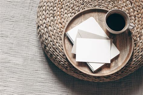 아침 식사 문구 모형 장면입니다 등나무 짚 퍼프에 놓인 나무 트레이에 커피 한 잔 빈 인사말 카드 봉투 및 메모장 최소한의 현대 보헤미안 인테리어 평면 평신도 상단 보기
