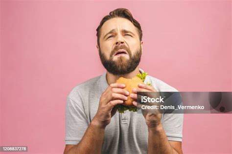 햄버거 한 조각을 들고 있는 청년 수염이 있는 규는 패스트푸드를 먹는다 햄버거는 도움이 음식 매우 배고픈 사람 다이어트 개념