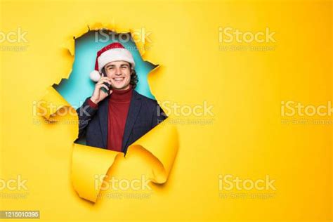 노란 종이 구멍을 통해 전화로 말하는 산타 모자를 쓴 청년 크리스마스 판매 12월에 대한 스톡 사진 및 기타 이미지 12월 겨울 구멍 Istock
