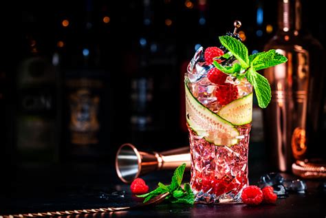 드라이 진 강장제 시럽 리치 주스 레몬 라즈베리 얇게 썬 오이 얼음을 곁들인 블랙베리를 곁들인 로즈 가든 칵테일 음료 검은색 바 카운터 배경 바 도구 및 병 0명에 대한