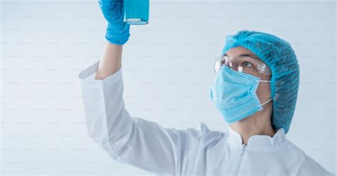 임상 실험을 하고 백신 용액을 검색하고 파란색 액체가 담긴 의료용 유리병을 들고 샘플을 확인하고 흰색 배경에 격리된 과학자 여성의 낮은 각도 보기 사진