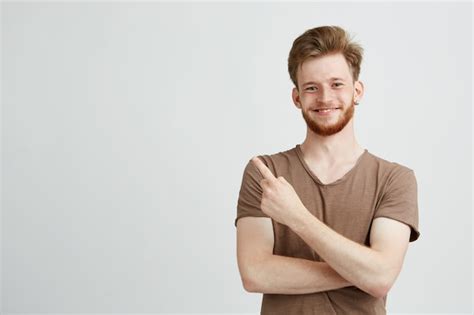Retrato Del Hombre Sincero Hermoso Joven Con La Barba Que Sonríe Señalando El Dedo En Lado