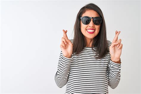 줄무늬 티셔츠와 선글라스를 착용한 중국 여성은 고립된 흰색 배경에 서 서 있는 손가락으로 희망을 품고 눈을 감고 미소를 지었다 행운과 미신 개념 T 셔츠에 대한 스톡 사진