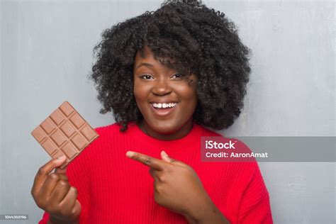 그런 지 회색 벽 매우 행복 손과 손가락으로 가리키는 바 초콜릿을 먹는 동안 젊은 아프리카계 미국인 여자 가리키기에 대한 스톡 사진 및 기타 이미지 Istock