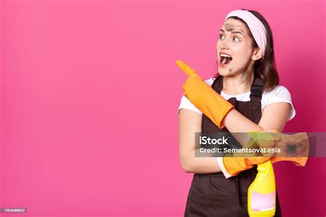 활기찬 날씬한 주부와 함께 활짝 열린 입 옆으로 찾고 손을 올리고 한 손에 수건 및 세제를 들고 집게 손가락으로 방향을 표시 합니다 광고 공간을 복사 합니다 가사 집안일에