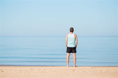 모래 위에 홀로 서서 따뜻한 여름 아침에 잔잔한 바다와 밝은 푸른 하늘을 응시하는 청년 정서적 긍정적 영감 텍스트 인용 또는 말을위한 빈 장소 다시 보기입니다 개념에 대한