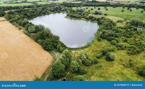 Aerial View Of A Lake Between Green Fields With Trees And Bushes In The