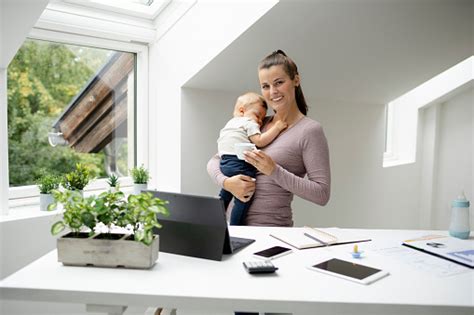 예쁜 젊은 여성 사업가가 직장 책상에 서서 잠자는 아들을 품에 안고 노트북 스마트 폰으로 작업합니다 가족에 대한 스톡 사진 및 기타 이미지 Istock
