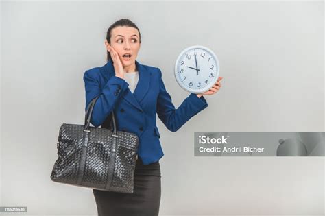 가방을 들고 정장 을 입은 젊은 교사는 흰색 시계를 들고 마치 시간을 잊어 버린 것처럼 무서운 얼굴 표정으로 그것을 보고있습니다 가방에 대한 스톡 사진 및 기타 이미지