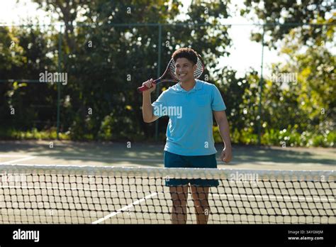 Mid Adult Man Standing Behind Tennis Net On Outdoor Court Holding