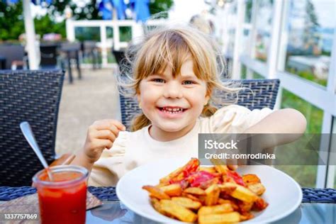 야외 테라스에 레스토랑에서 토마토 케첩과 감자 튀김을 먹는 행복 미소 유치원 소녀의 초상화 금발 머리를 가진 어린 아이는 건강에 해로운 패스트 푸드 또는 신선한 준비 점심을