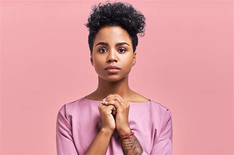 쾌활한 아프리카 계 미국인 여성의 스튜디오 샷은 턱 근처에 손을 잡고 광범위하게 미소 그녀의 생일에 친구가 준비 한 놀라움을 기대 분홍색 배경에 고립 검은색에 대한 스톡