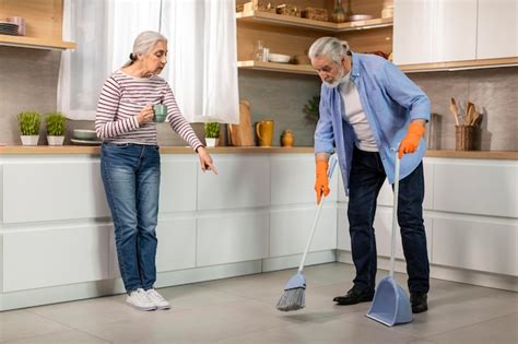 Mulher Idosa Limpando O Marido Na Cozinha Apontando Para A Poeira No