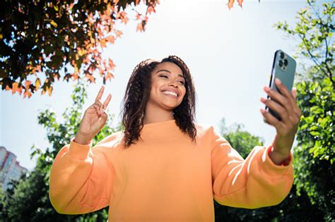 사랑 스럽다 달콤한 아가씨 오렌지 스웨터를 입고 V 기호 압정 셀카 현대 장치 야외 도시 도시 공원의 사진 25 29세에 대한 스톡 사진 및 기타 이미지 Istock