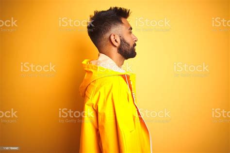 고립된 노란색 배경 위에 서있는 비옷을 입은 젊은 인도 남자는 자신감을 가지고 자연스러운 얼굴로 프로필 포즈를 취합니다 가을에 대한 스톡 사진 및 기타 이미지 Istock