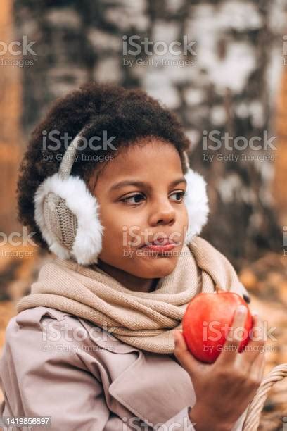 สาวแอฟริกัน อเมริกันน่ารักกินแอปเปิ้ลที่ปิกนิกในสวนฤดูใบไม้ร่วง ความหลากหลาย แนวคิดฤดู ภาพสต็อก